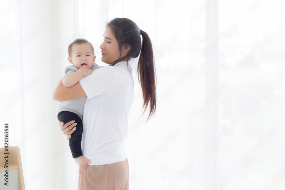 Young asian mother holding little baby girl and walking together in the bedroom at home, mom ...