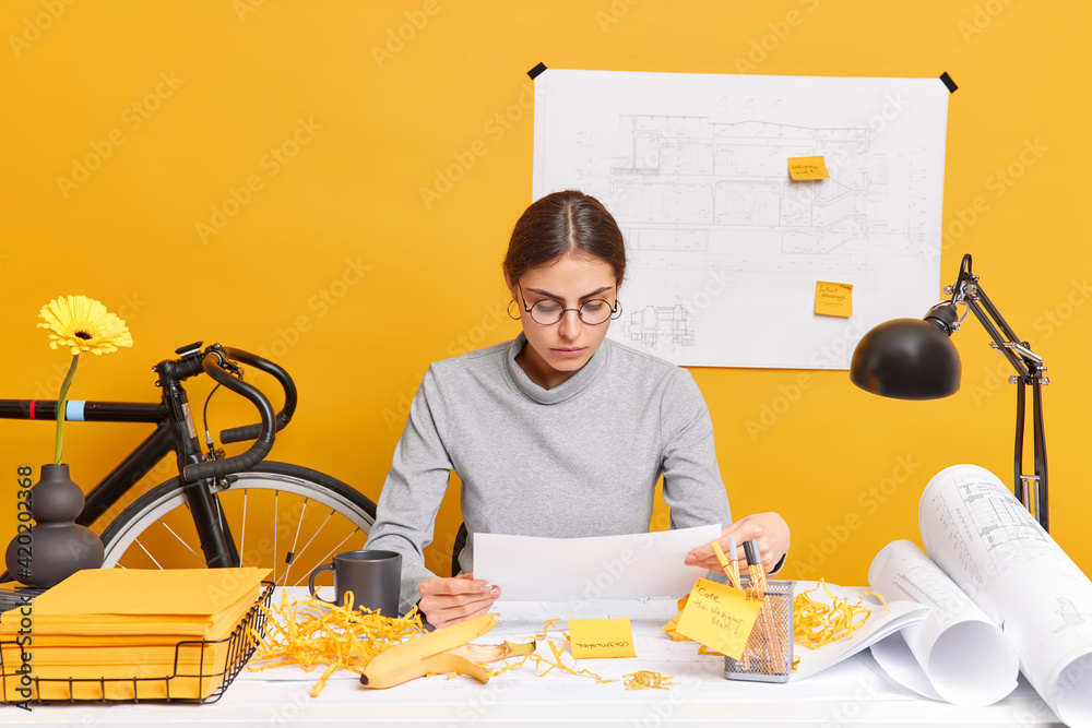 Serious professional female architect concentrated in paper poses at ...