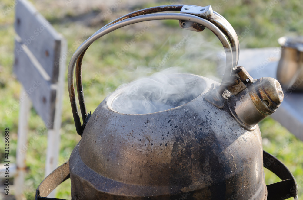 Water boils in a metal kettle in the garden. Cooking outdoors during ...