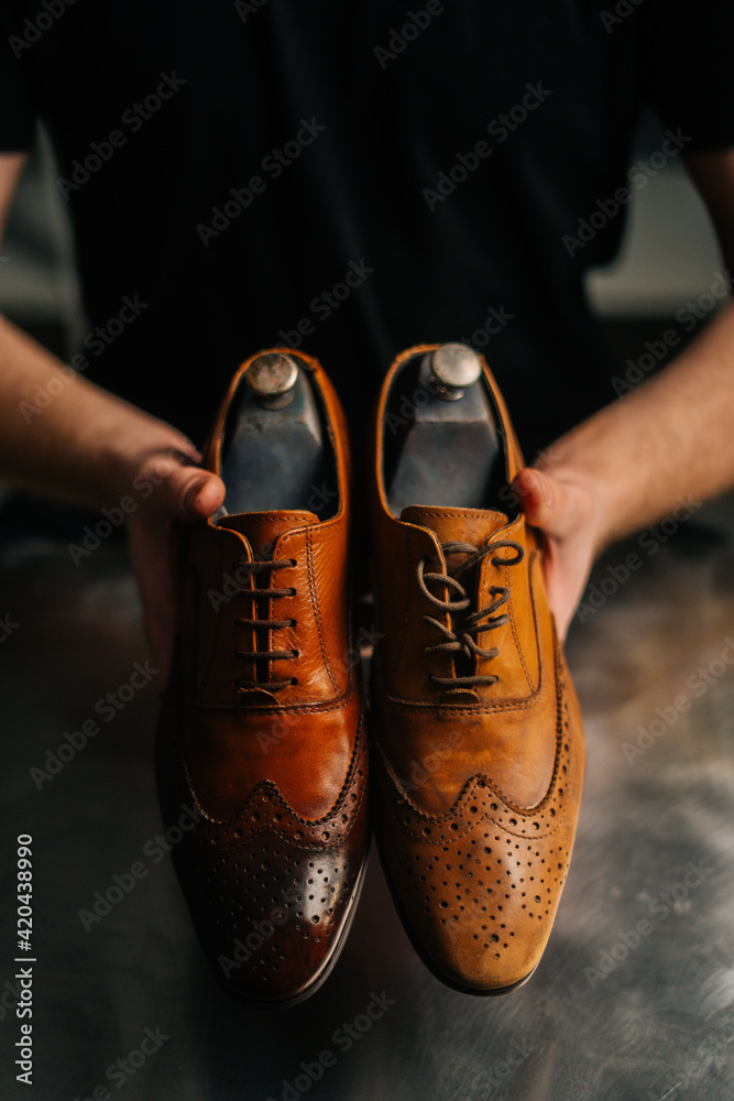 Close-up hands of male shoemaker holds old light brown leather shoe and ...