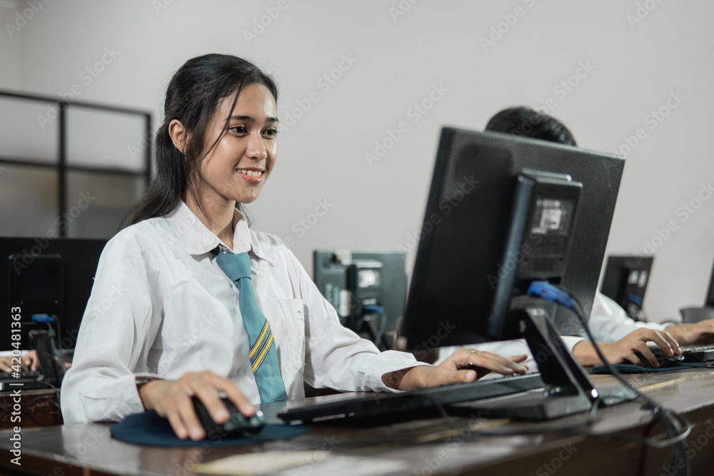 female high school students smile while using a computer pc with their ...