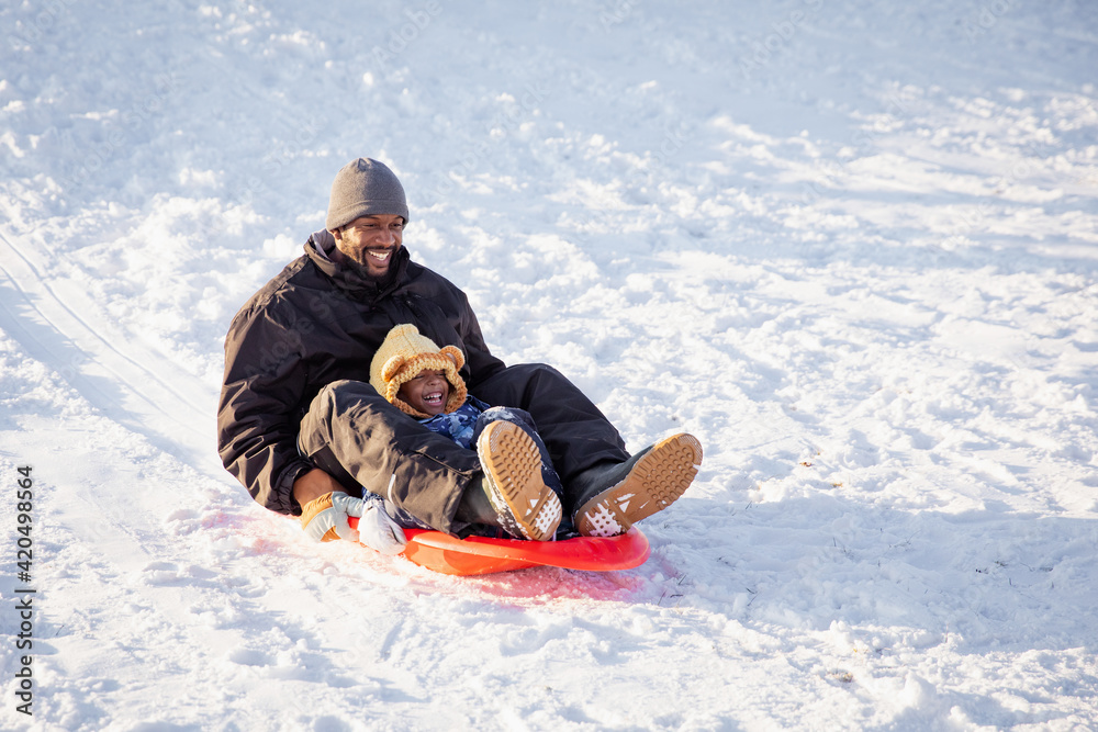 Cute child happily riding down a hill on a toboggan sled with his dad ...