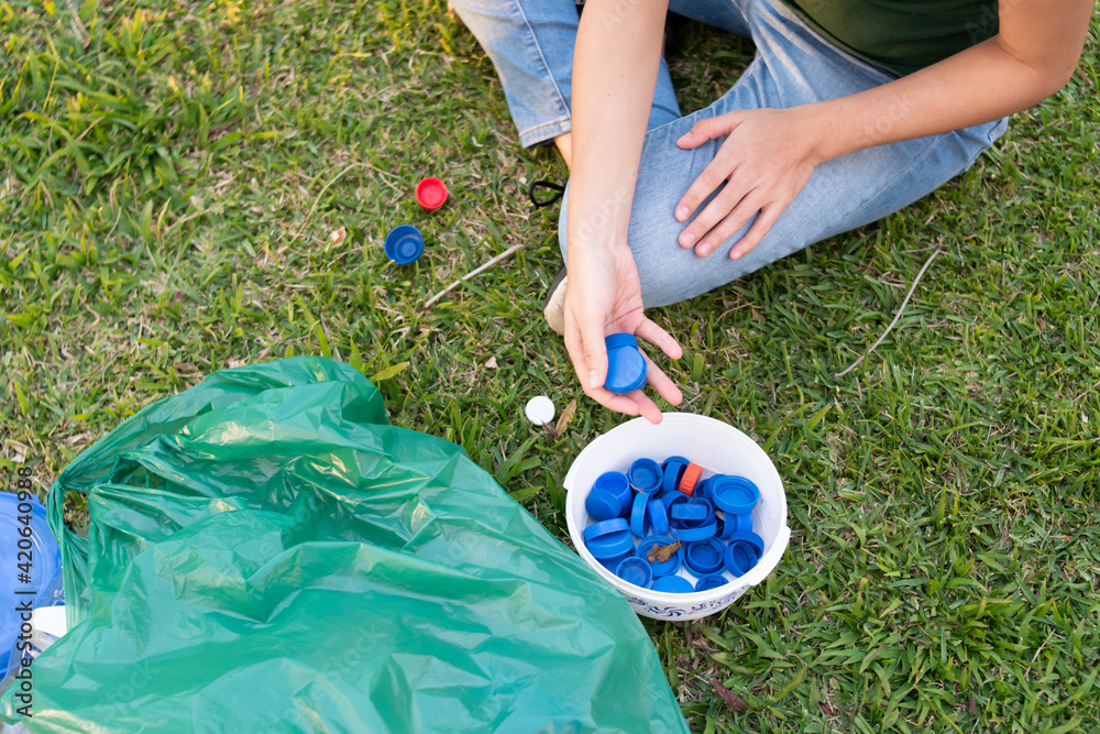 Recycle, girl sitting on the green grass collecting caps and plastic ...
