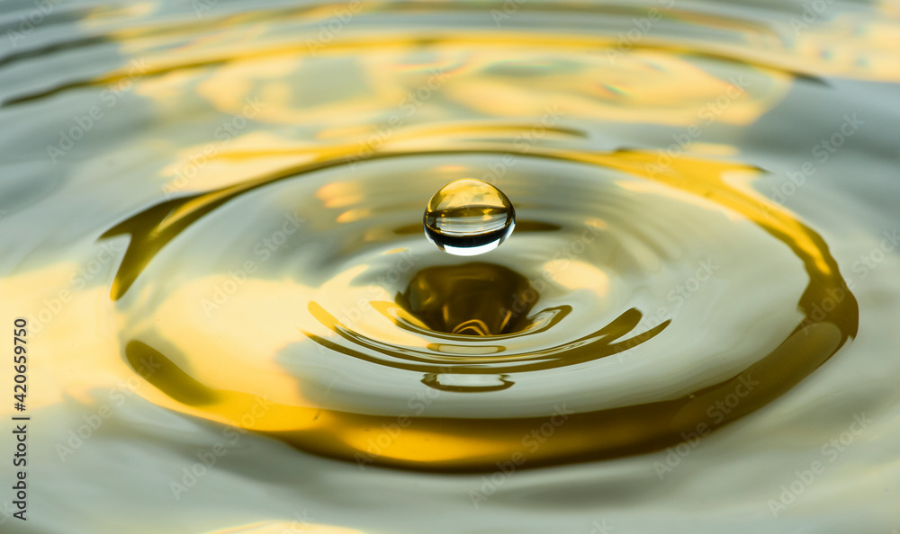 Water drops frozen at high speed in golden pool of water showing ...