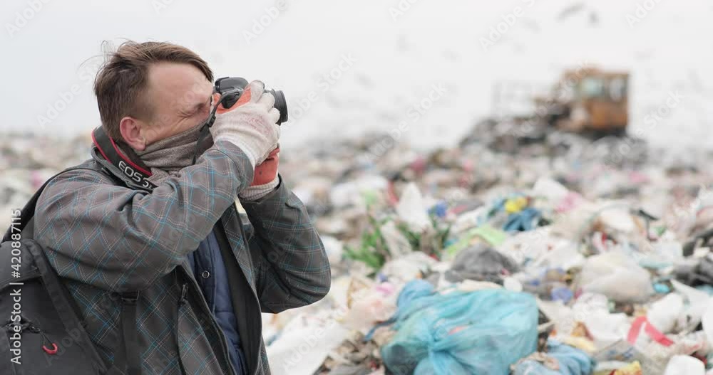 male photographer with a large black backpack stands in a landfill and ...