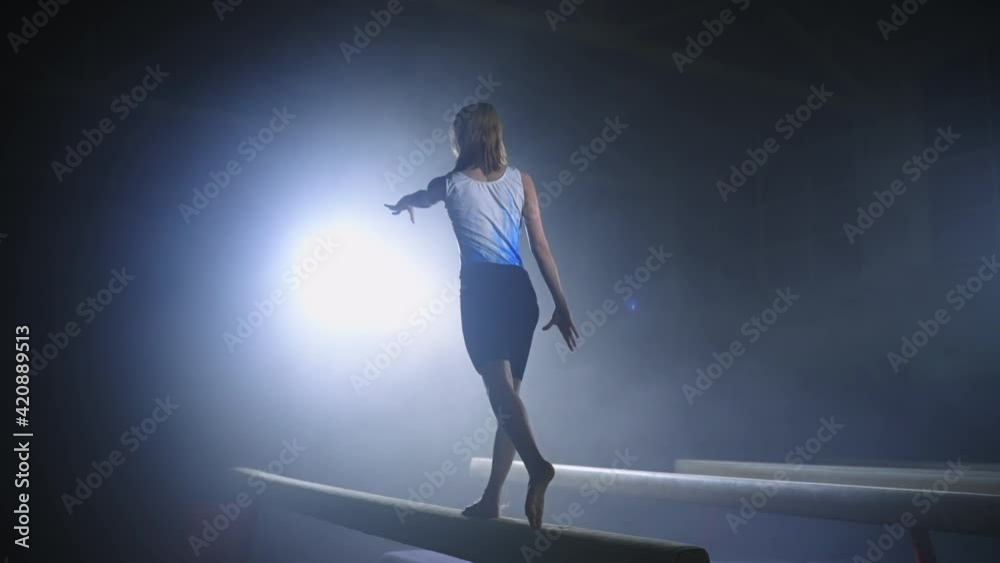 talented female gymnast is training alone in gymnastic hall at night ...