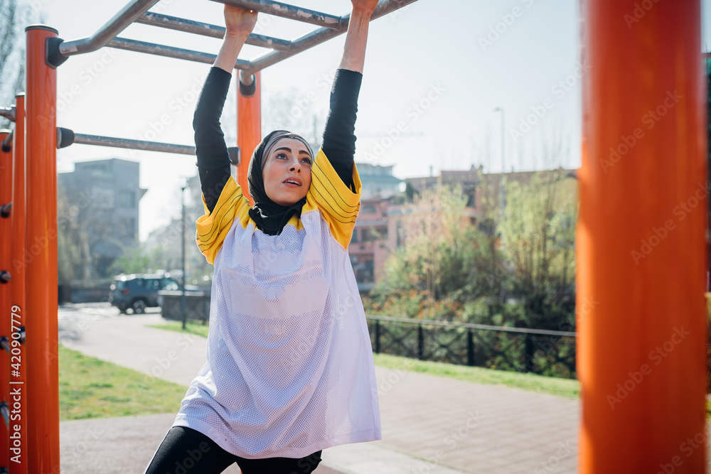 Calisthenics class at outdoor gym, young woman hanging from exercise ...