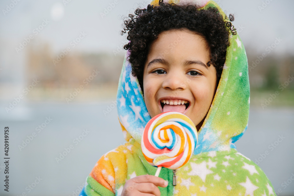 Black boy wearing pajamas, smiling, sucking on a giant lollipop . In a ...