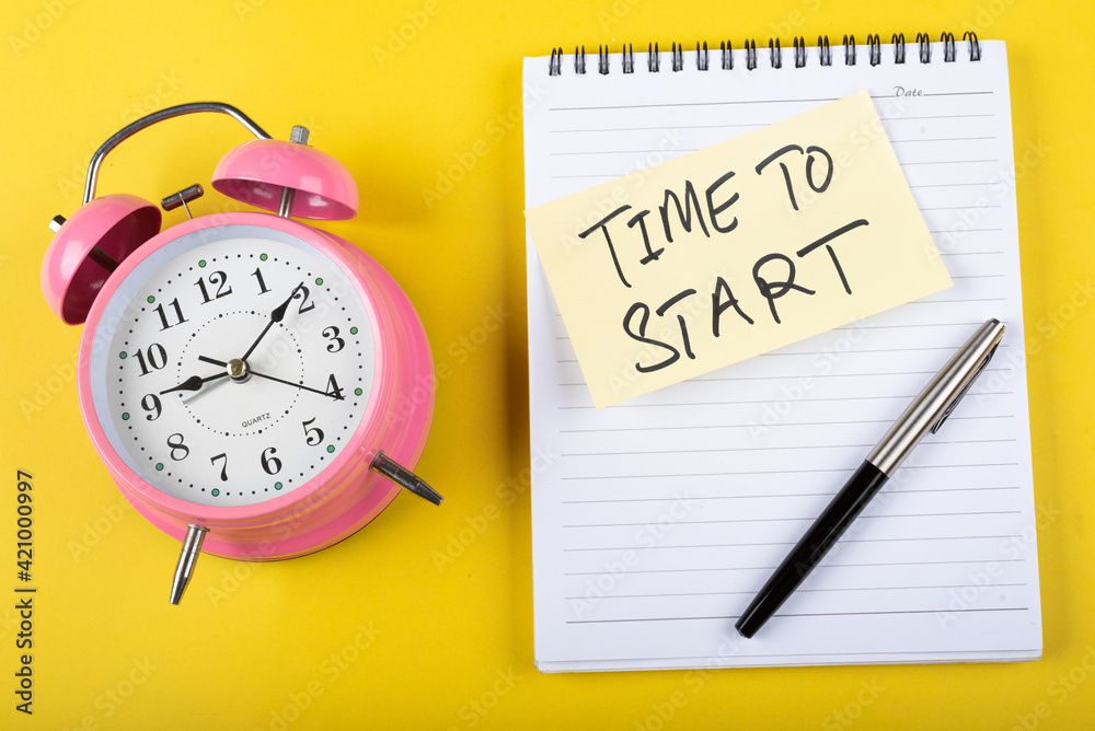 A table clock with Time to start words Written on a sticky note with ...