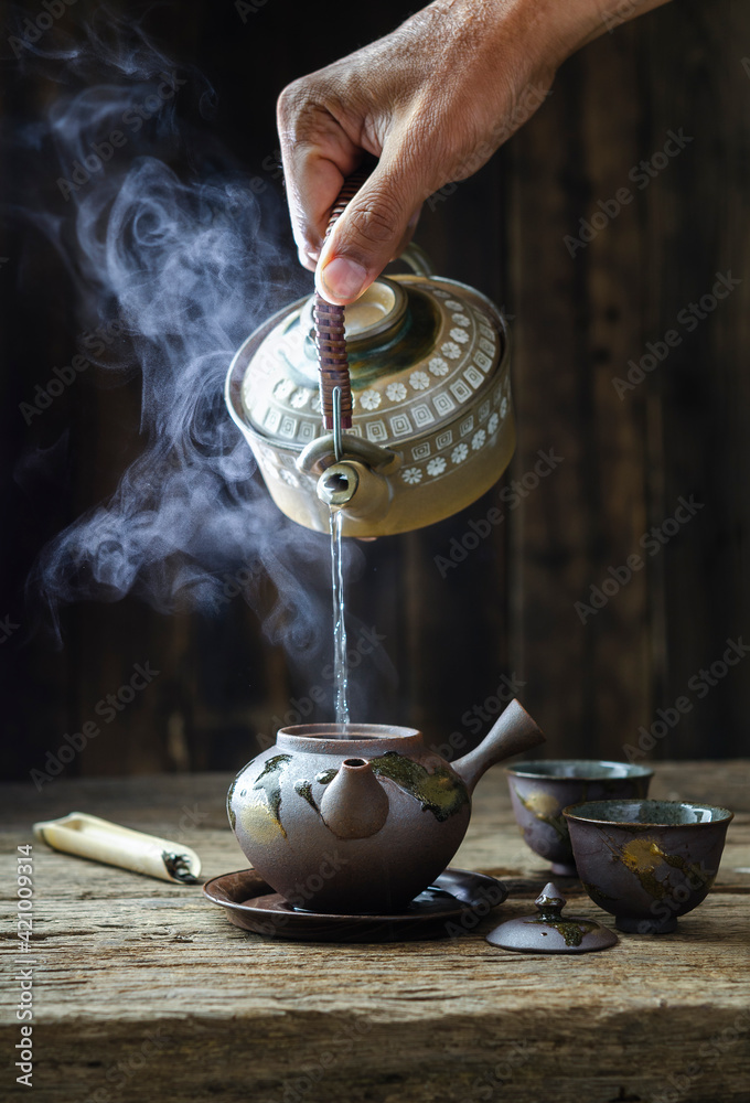 pouring hot water from a pot into teapot steam is over the teapot ...