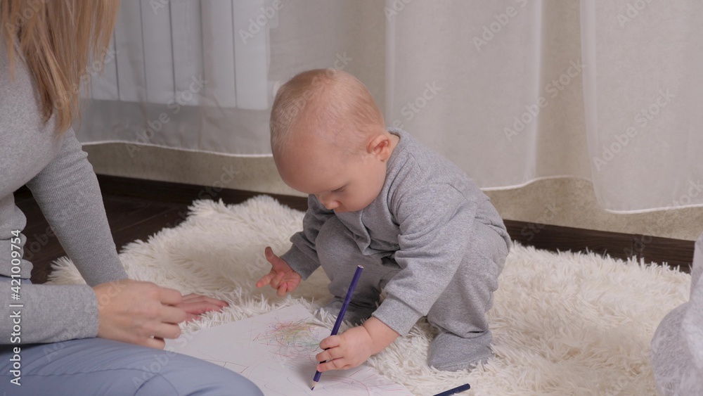 A baby daughter enthusiastically draws with yellow pencil on sheet of ...