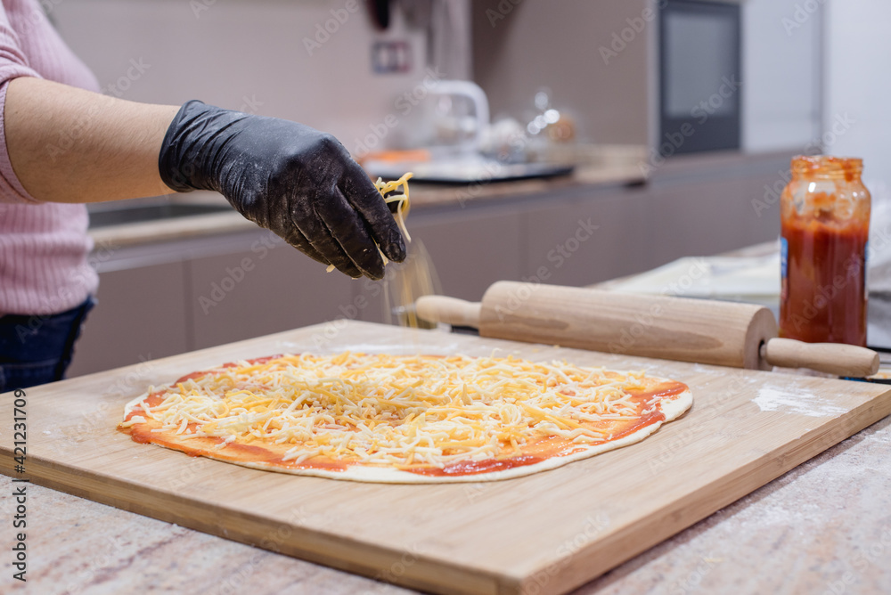 Detalle de una mujer echando queso mozzarella en la masa de una pizza ...