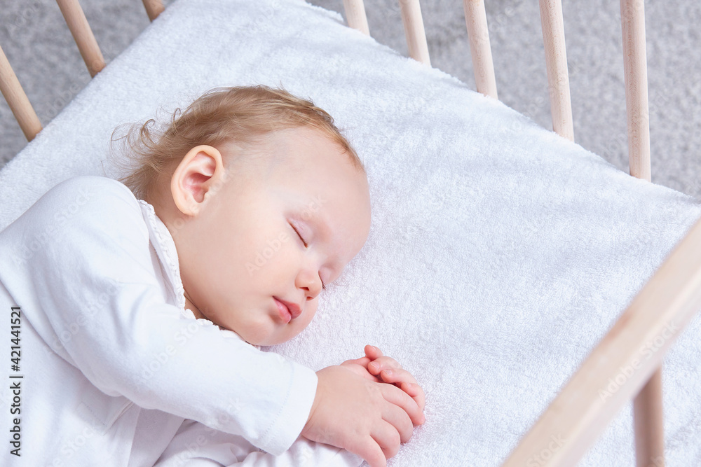 The baby sleeps safely and sweetly in his wooden crib on a terry sheet ...