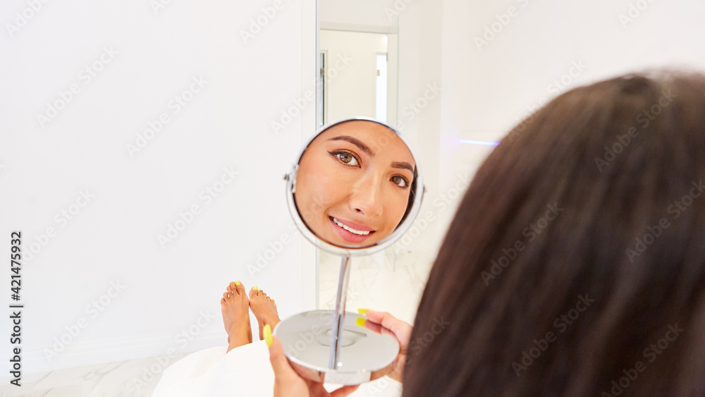 Young woman looks at her face in a mirror Stock Photo | Adobe Stock
