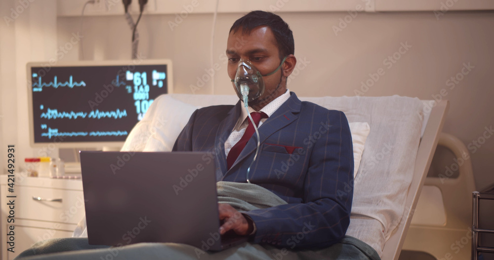 Indian businessman with oxygen mask in suit working with laptop lying ...