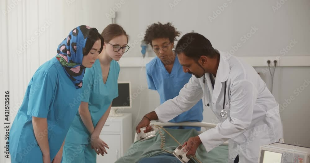 Doctor using defibrillator on patient while medical team standing ...