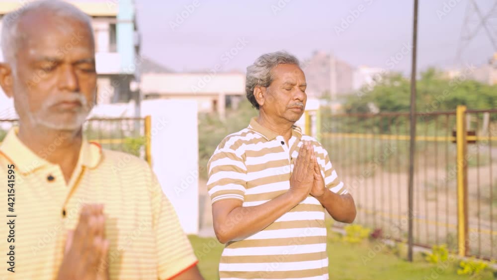 Rack focus of two old men with closed eyes and namaste posture doing ...