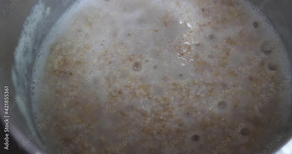 Boiling steel cut oats in pan. Bubbles pop in the oatmeal being cooked ...