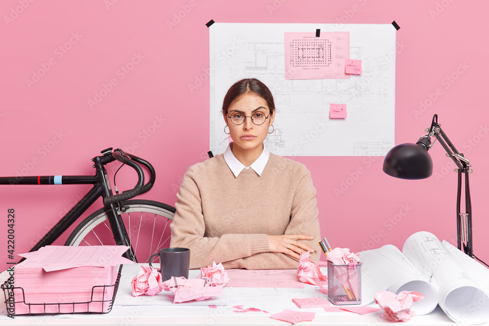 Serious female designer poses at office desktop prepares architectural ...