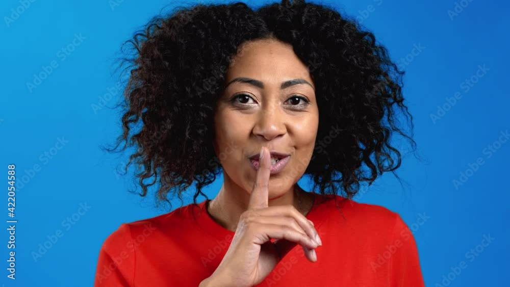 Smiling African Woman With Curly Hair Holding Finger On Her Lips Over