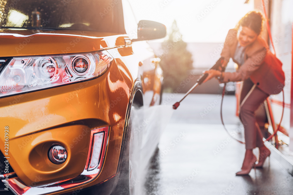 Businesswoman washing car at car wash station using high pressure water ...