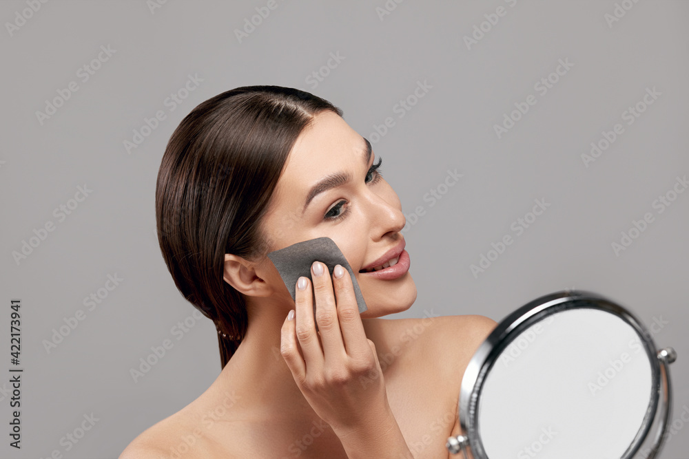 Skin care. Young woman removing oil from face using blotting papers ...