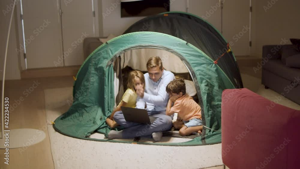 Dad and children watching horror movie on laptop in tent. Daddy and ...