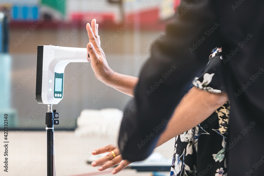 Customer with protective mask raised hand at digital thermometer with ...