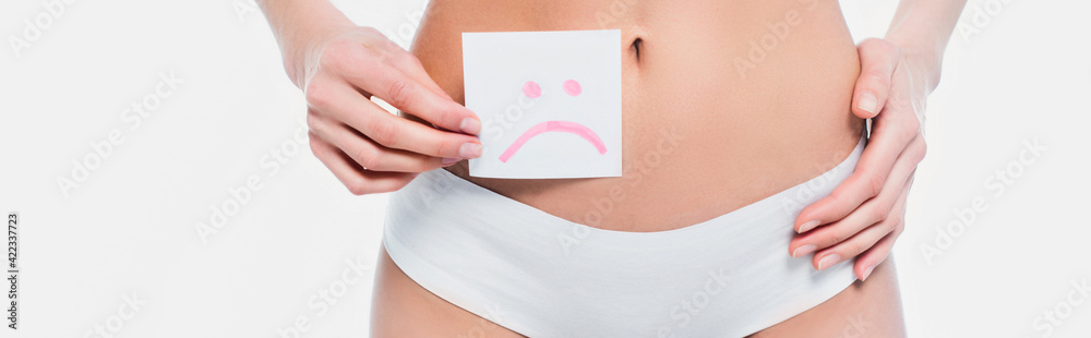 Cropped view of woman in panties holding card with sad emoticon isolated on white, banner Stock ...