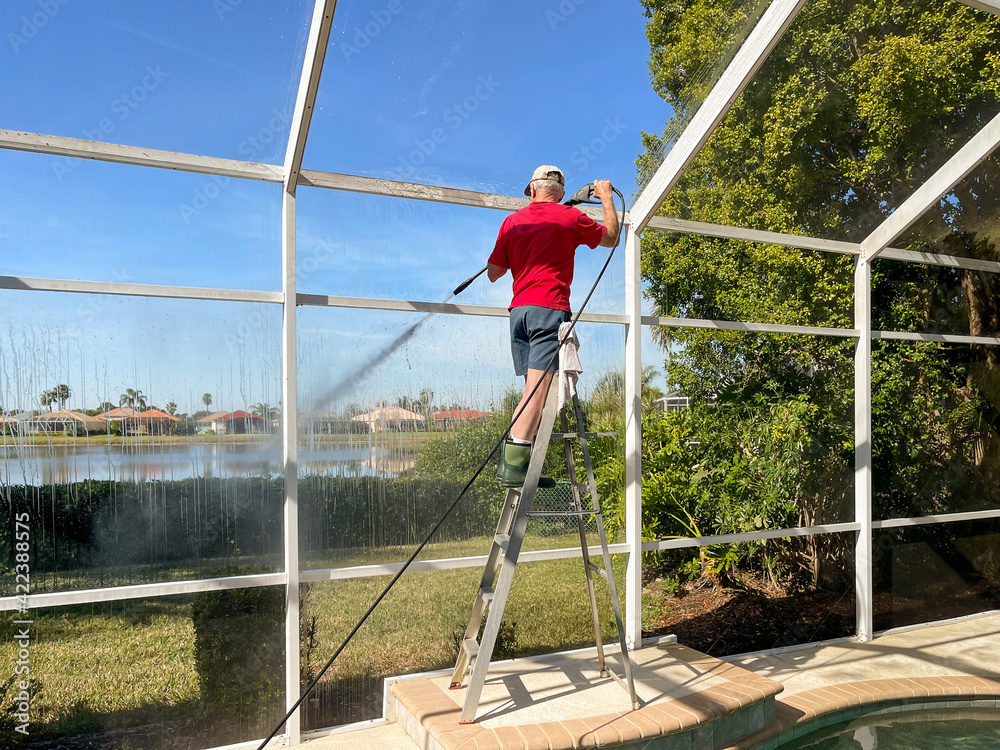 Handyman cleaning outdoor screen pool cage enclosure with power washer ...