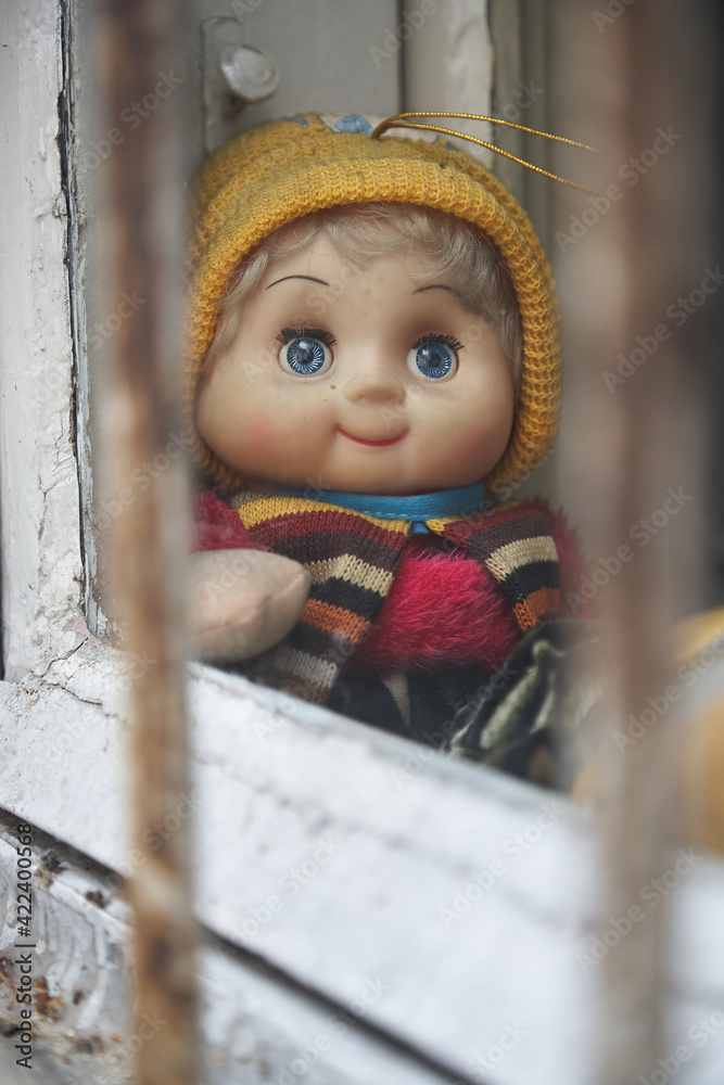 Doll looks out of the window. Her eyes are wide open and she wears a ...