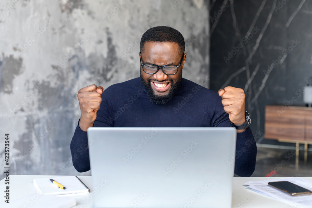 Excited African-American young businessman screams yes, sitting at the ...