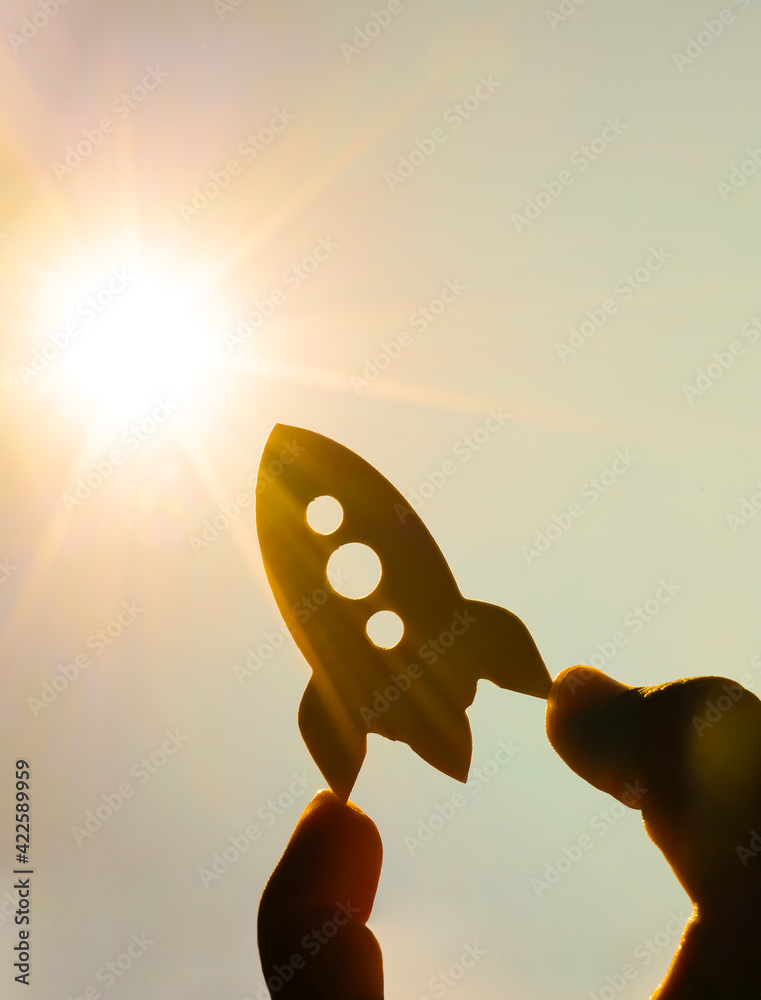 male hand hold rocket sing, symbol against the blue sky and sun rays ...