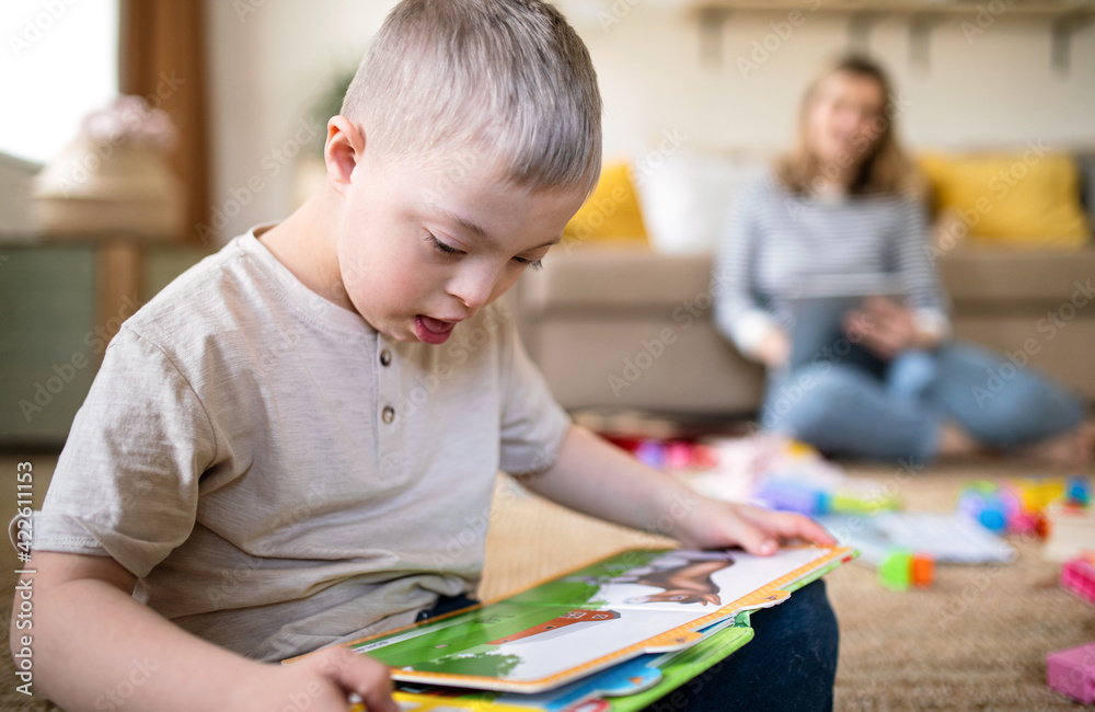 Down syndrome child reading book at home, mother working in home office ...