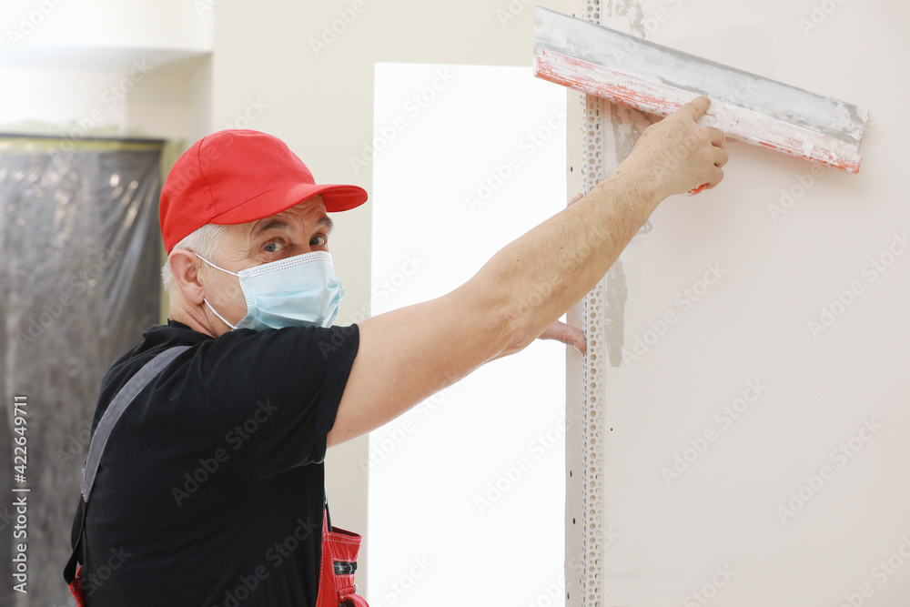 Builder in protective mask using a trowel to add plaster. Plastering ...