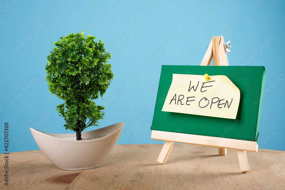 we are open written on a sticky note on a mini green notice board with ...