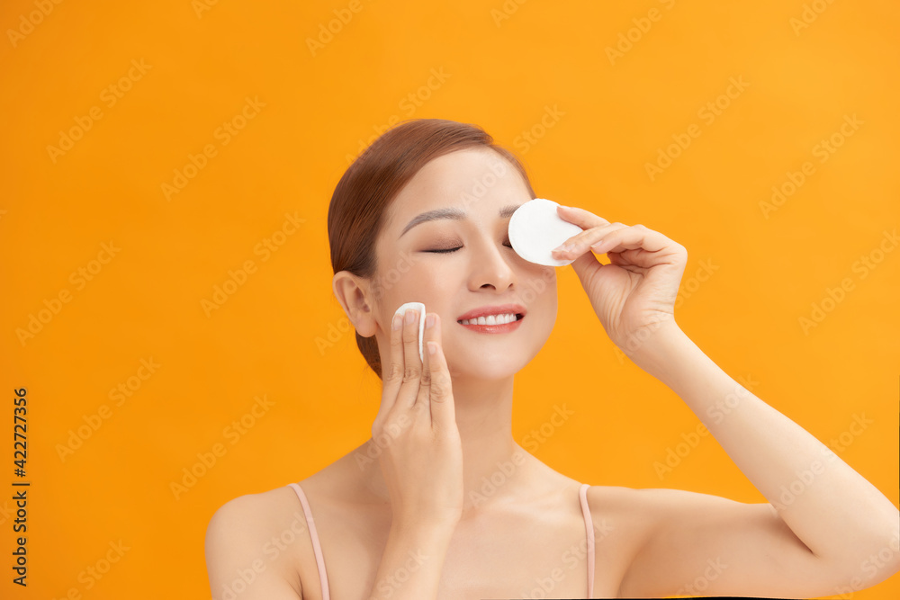 Beautiful woman removing her makeup using a cotton round over a white ...