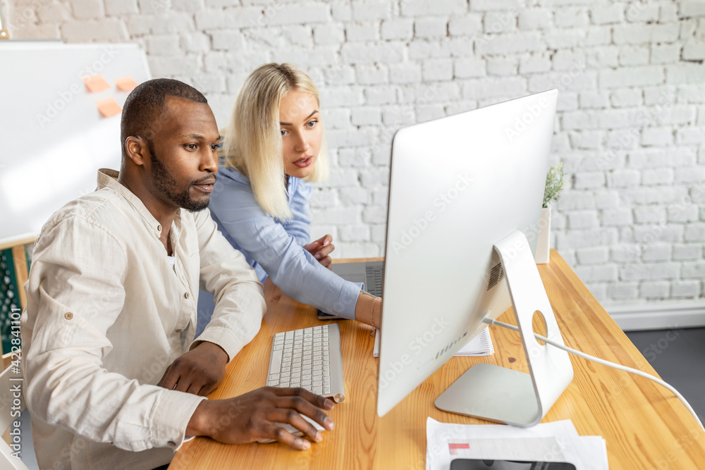 Focused young adult colleagues sitting at the desk, using computer ...