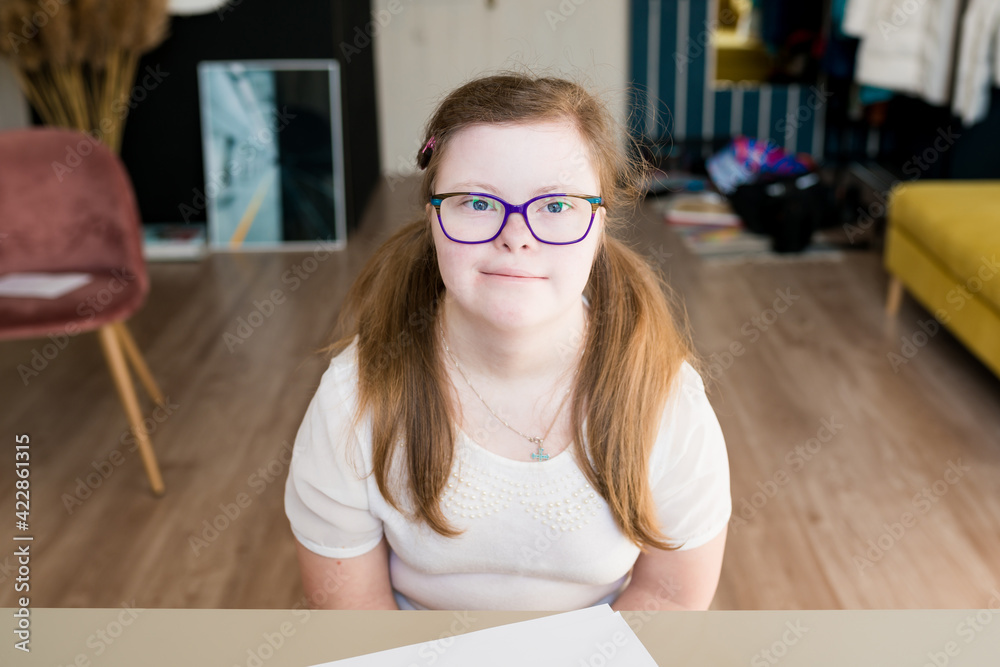 Portrait of cute teenager girl with Down syndrome sitting at home and ...