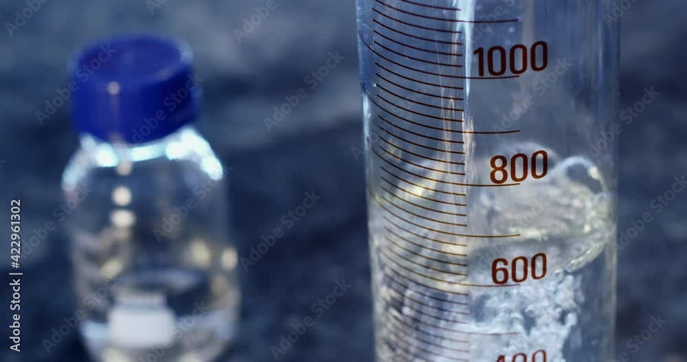 A transparent liquid is poured into a graduated chemical cylinder ...