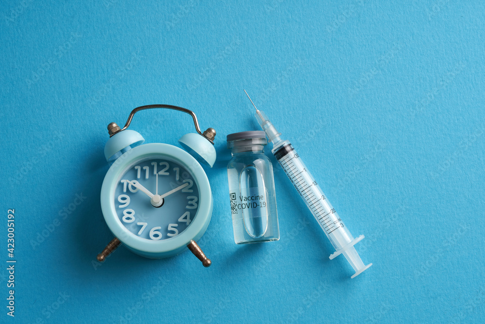 medical vaccine vials and alarm clock over blue background. time to ...