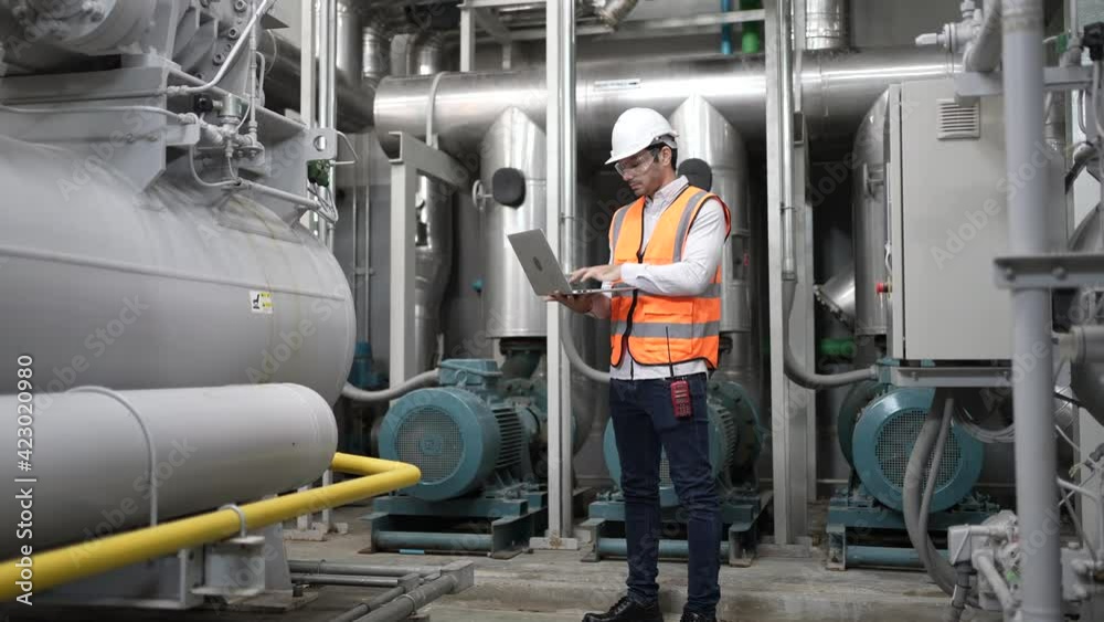 Professional worker of modern factory using laptop controlling program to automatic machinery ...