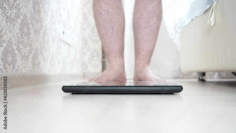 Close-up of a slender man with bare legs taking a step on the scale ...