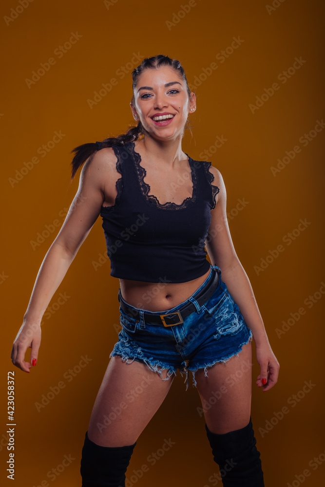 Young girl in denim shorts and black crop top posing on an orange light ...