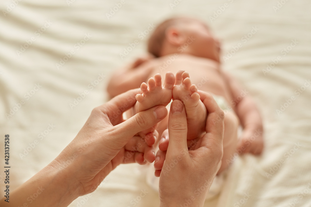 Faceless person making baby massage for infant lying on bed, mommy ...