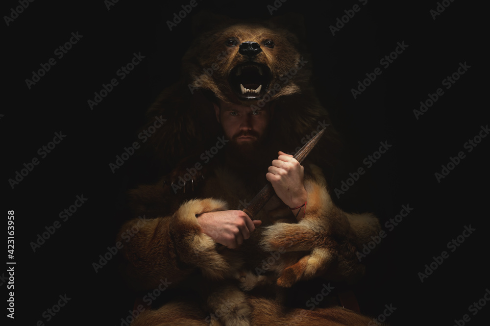 A male shaman werewolf in the skin of a bear sits in a dark room and ...