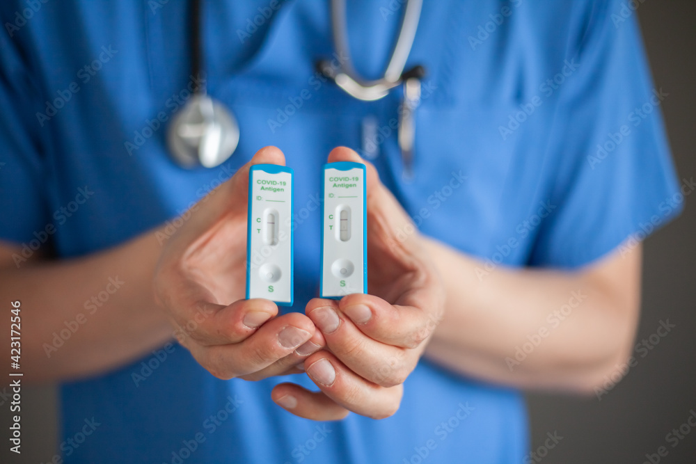 The doctor with stethoscope holds a negative and positive antigen tests ...