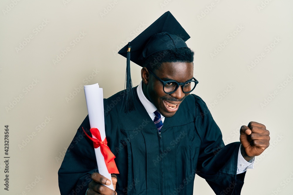 Handsome black man wearing graduation cap and ceremony robe holding ...