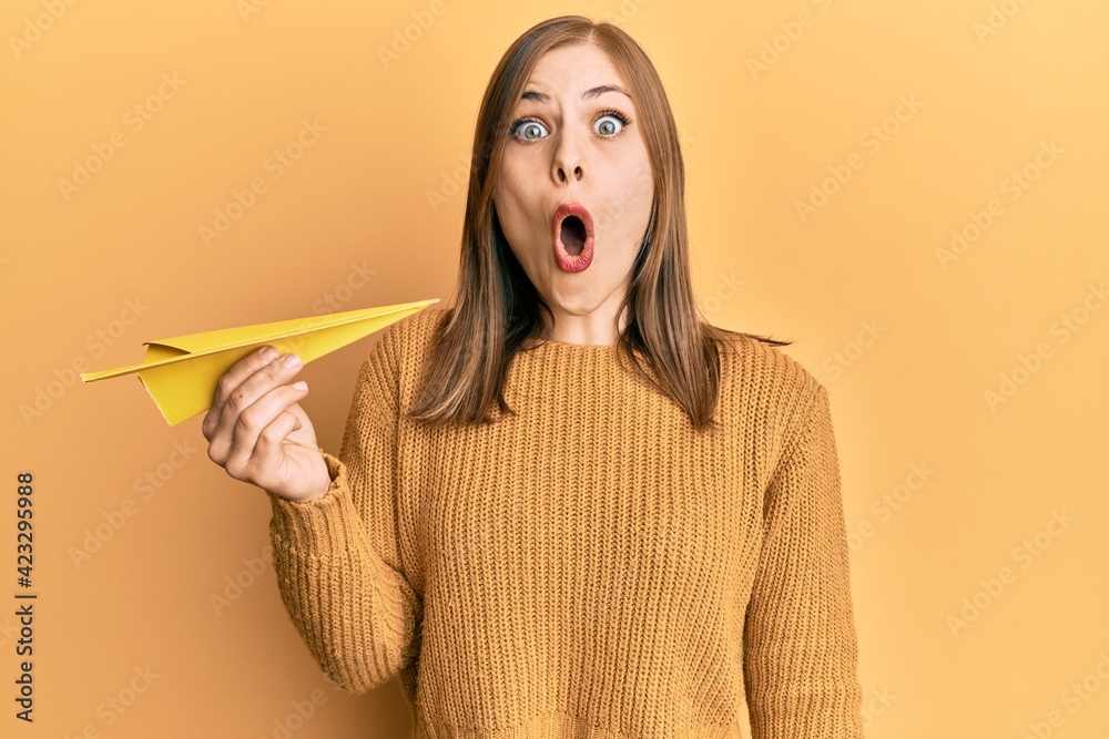 Beautiful caucasian woman holding paper airplane scared and amazed with ...