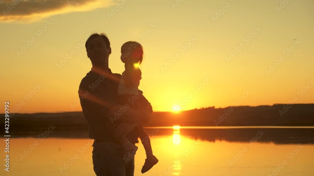 Happy family dad and baby, daughter hugging on the lake at sunset ...